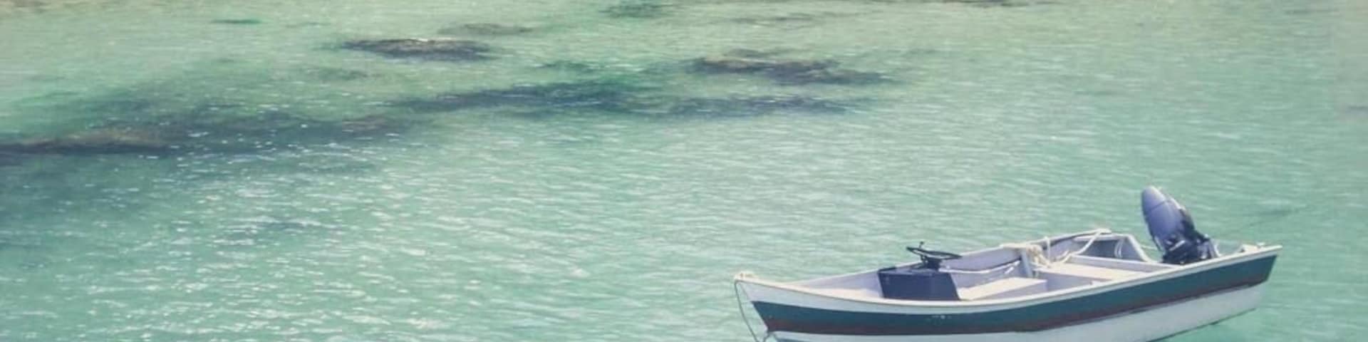 Um pequeno barco ancorado em águas turquesa cristalinas, com uma costa rochosa ao fundo.