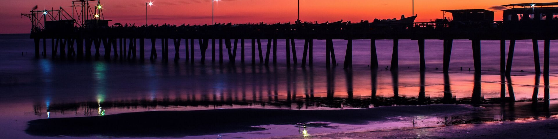 Um cais se estendendo sobre águas calmas ao pôr do sol, com um céu roxo.