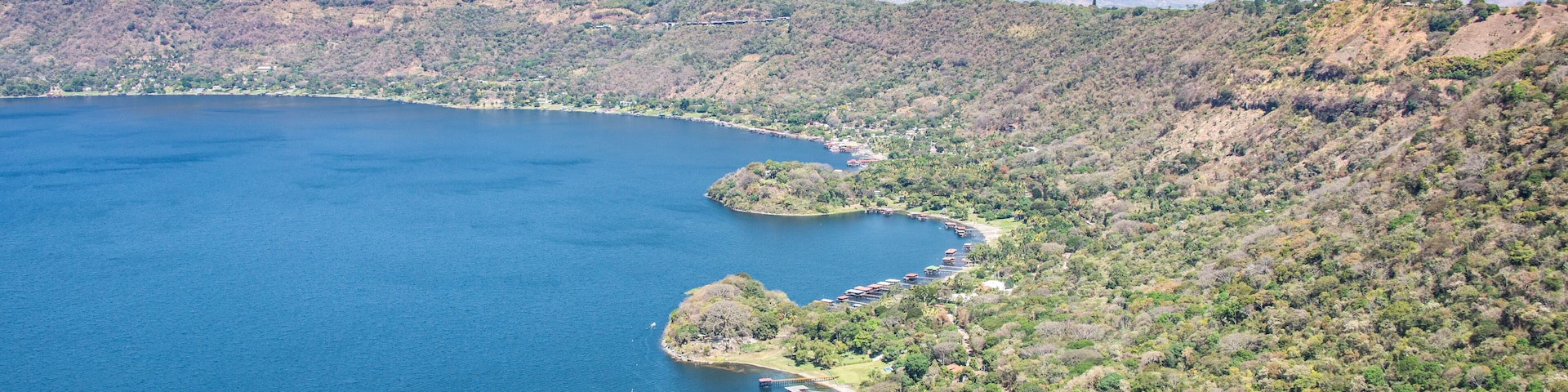 Paisagem costeira com uma extensa área de água, colinas verdes e céu claro.
