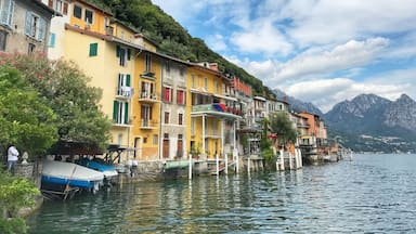 Uma pitoresca vila à beira do lago com edifícios coloridos, barcos e montanhas ao fundo.