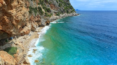 Paisagem costeira com falésias rochosas, águas turquesas cristalinas e uma ilha ao longe.