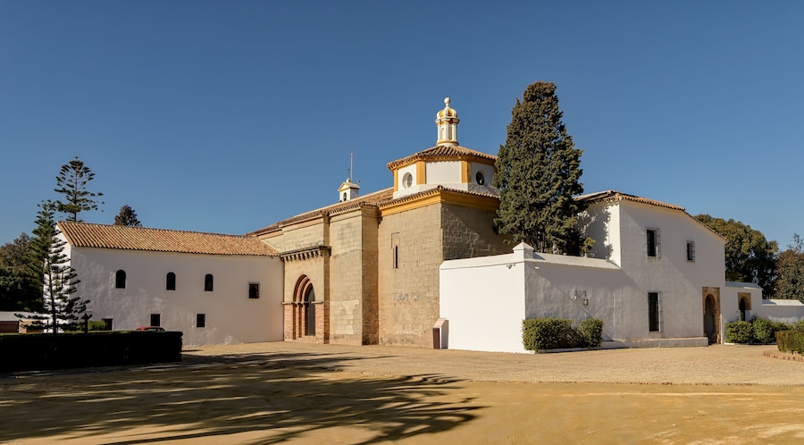 Uma igreja histórica com um campanário, rodeada por árvores e um céu claro.