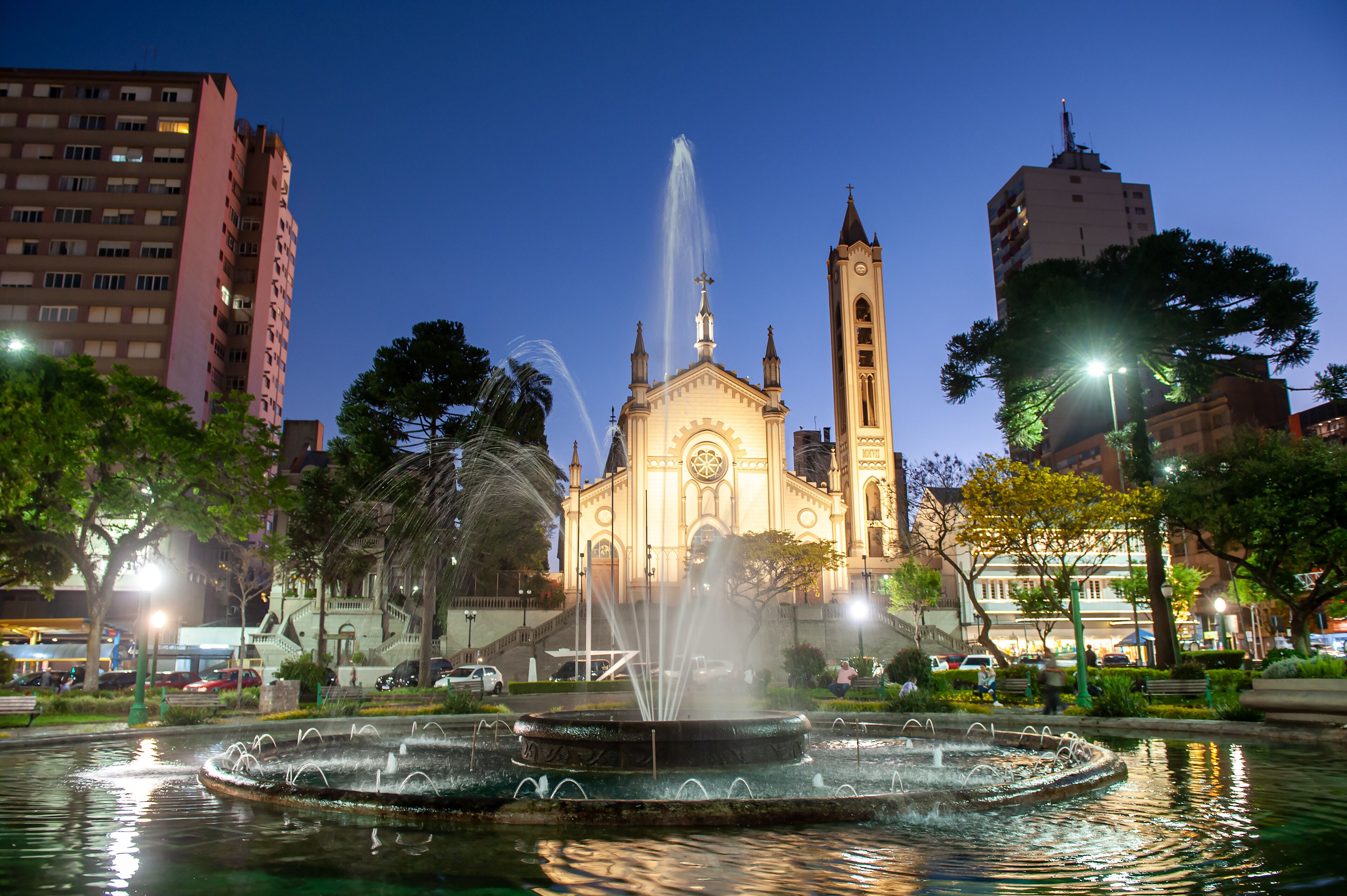 Uma igreja com uma alta torre de sino e uma fonte em primeiro plano.