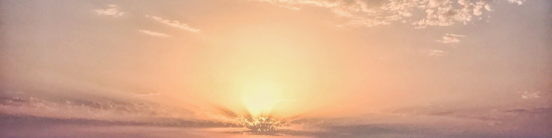 Cena de praia com pôr do sol, dois guarda-sóis e uma pessoa caminhando.
