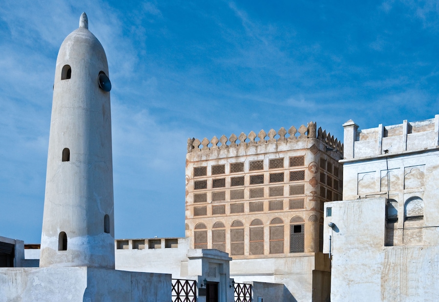 Uma torre alta e branca com janelas em arco e um edifício com fachada ornamentada.