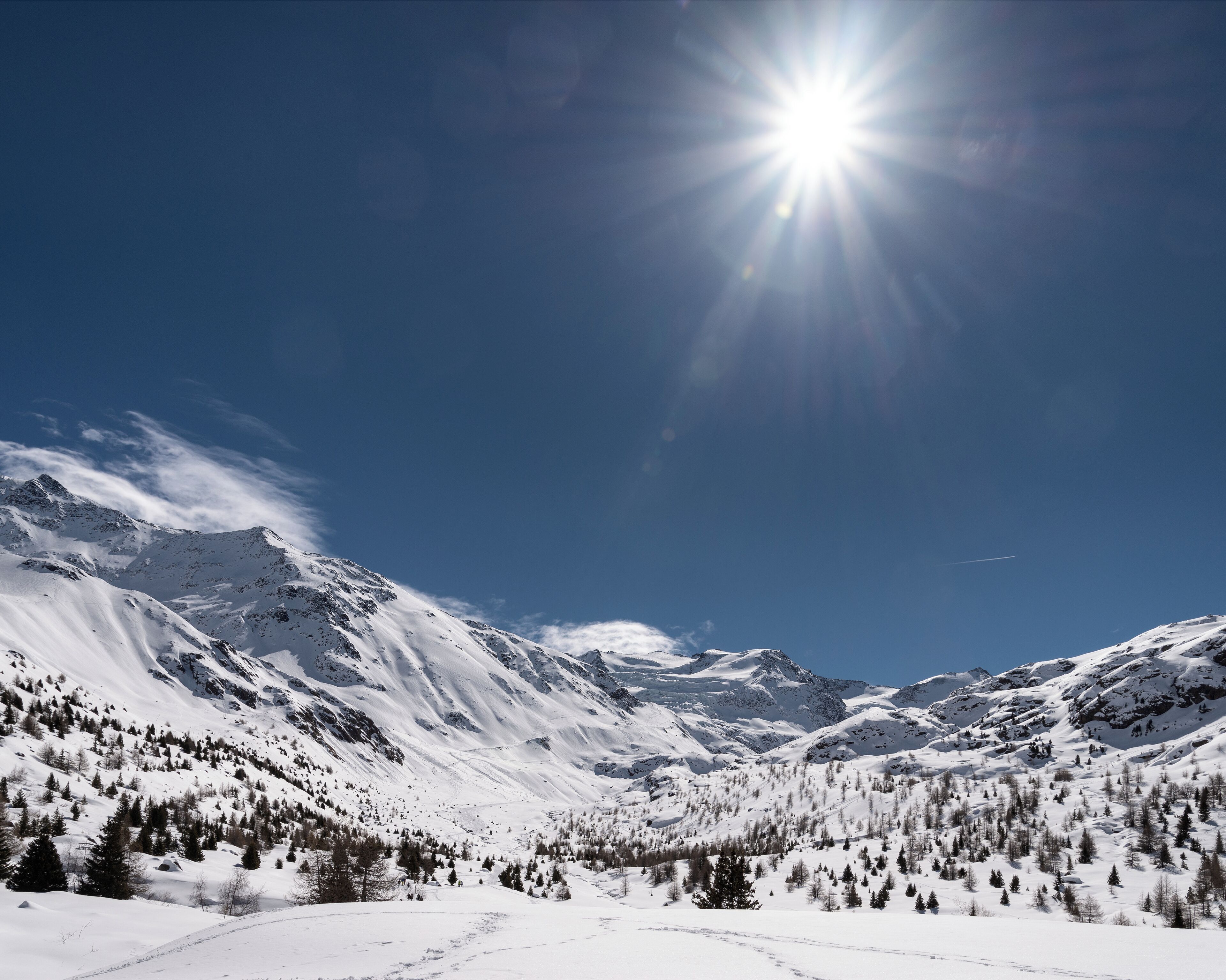 Paisagem montanhosa coberta de neve, com céu claro e sol brilhante.