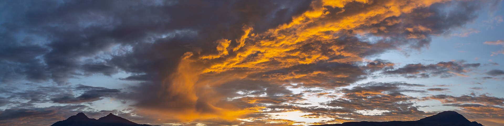 Pôr do sol sobre montanhas com uma formação de nuvens dramática.