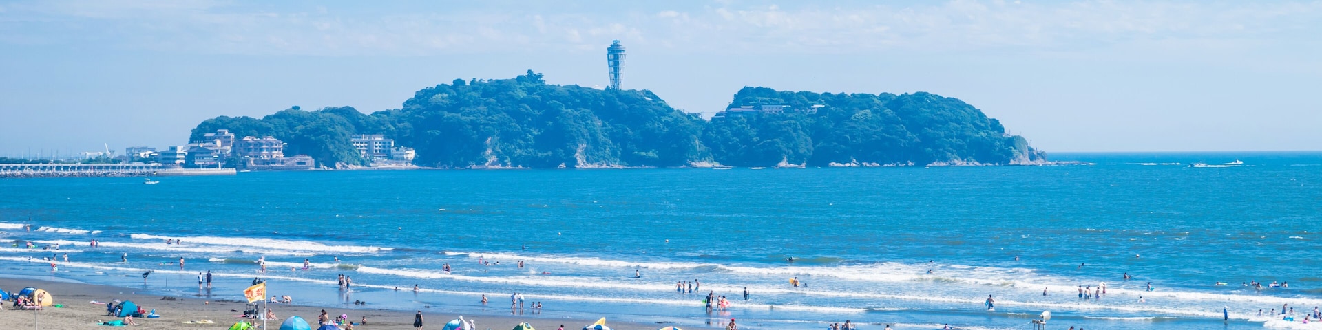 Uma praia com tendas, guarda-sóis e um farol ao longe.