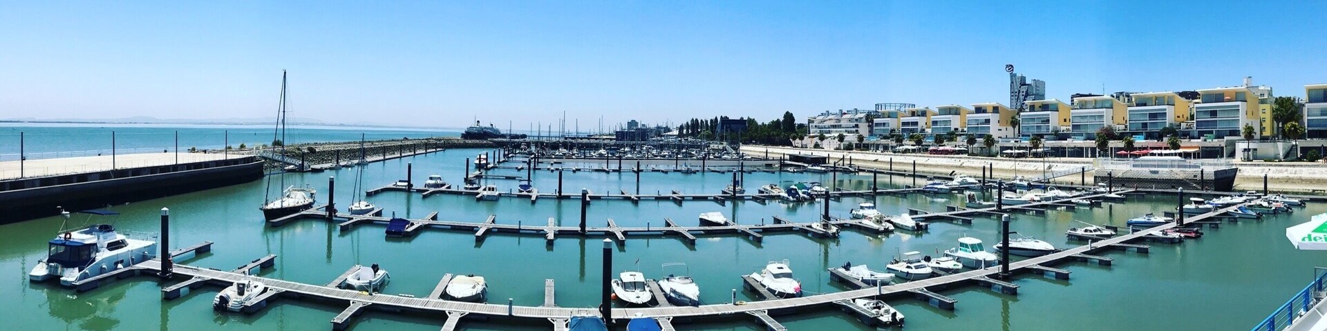 Marina com barcos atracados, céu azul límpido e edifícios ao fundo.