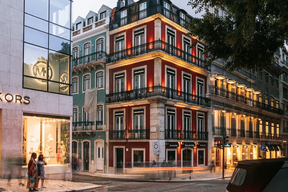 Uma rua com uma loja Michael Kors e um edifício Maria João Batista.