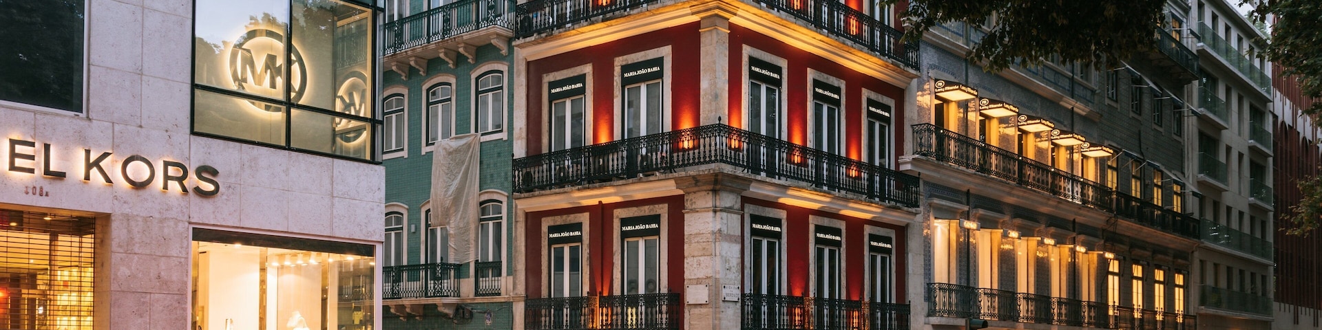 Uma rua com uma loja Michael Kors e um edifício Maria João Batista.