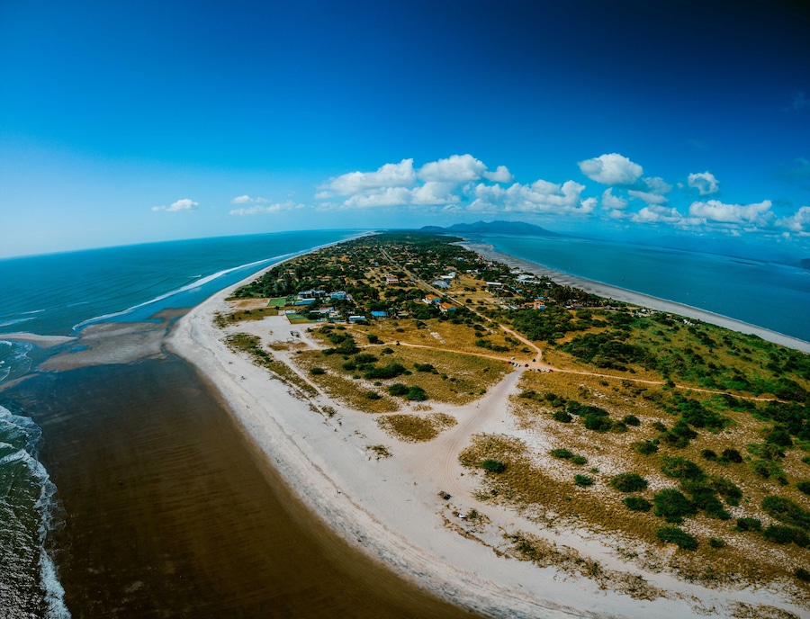 Paisagem costeira com uma praia, um pequeno povoado e um céu azul límpido.