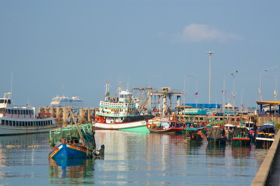 Um porto com vários barcos, incluindo um navio grande ao fundo e barcos menores atracados no cais.