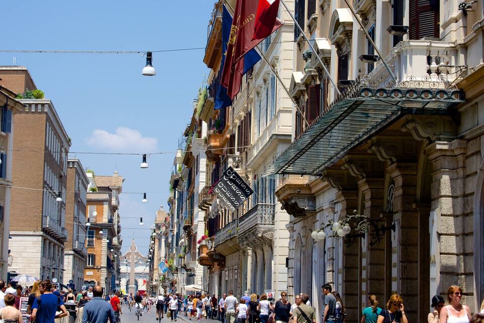 Uma rua movimentada com edifícios históricos, céu azul límpido e uma multidão de pessoas.