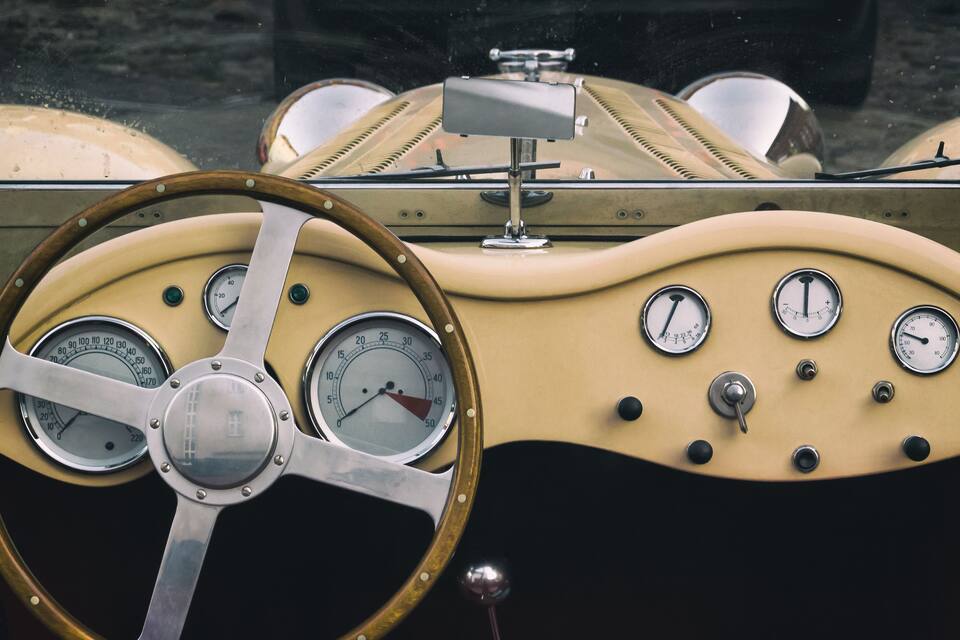 Volante e painel de um carro antigo com vários indicadores.