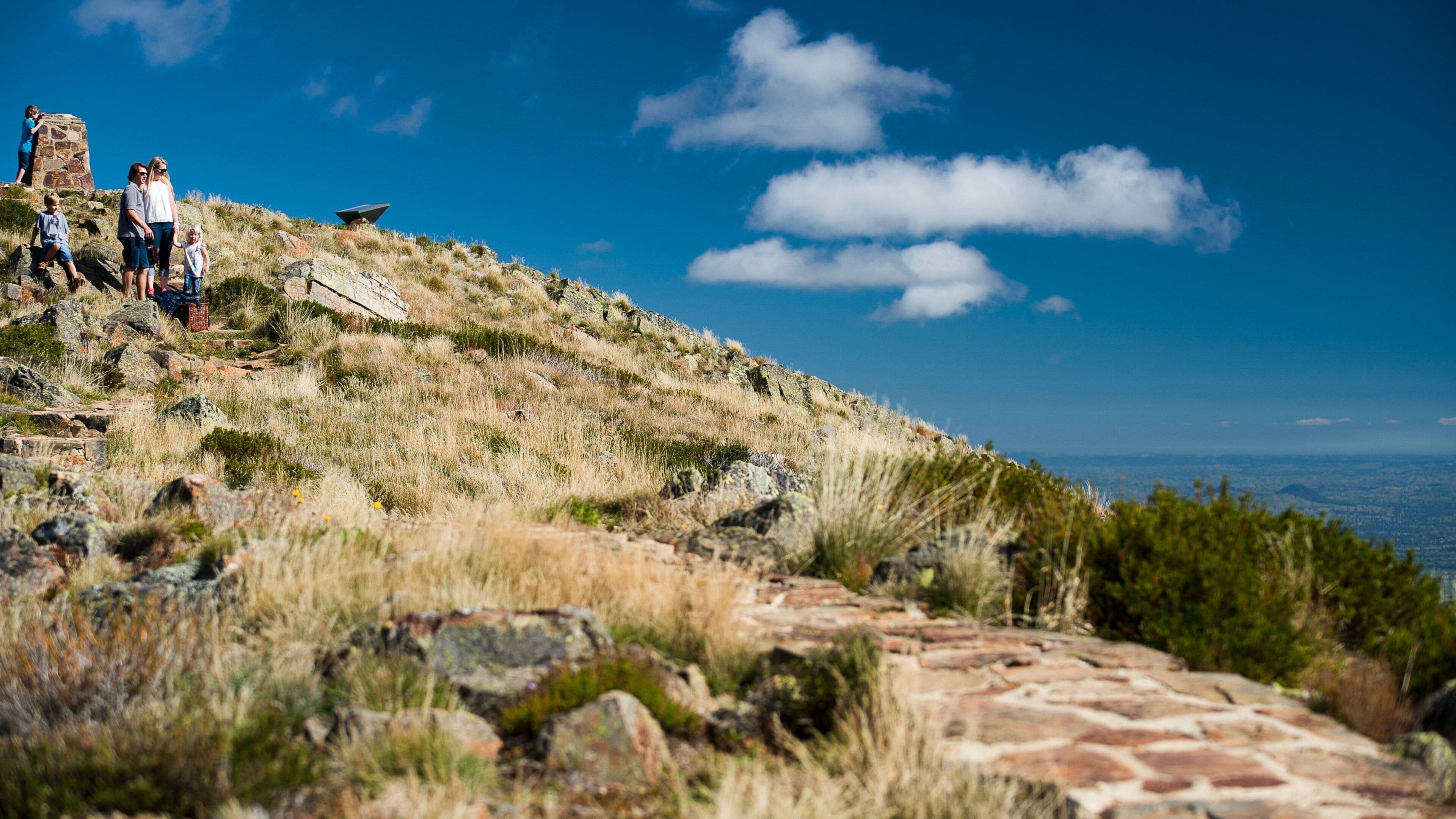 Uma encosta rochosa com um caminho de pedra, uma construção de pedra e um céu azul claro com nuvens.