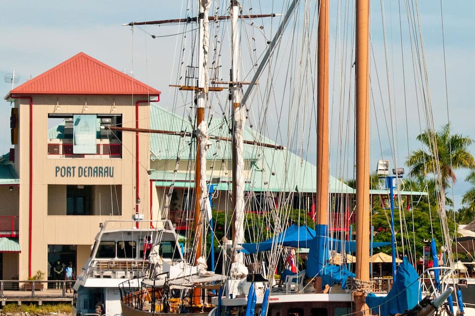 Um porto com um navio à vela alto chamado "Whale Tale" atracado ao lado de um edifício com a inscrição "Port Denarau".