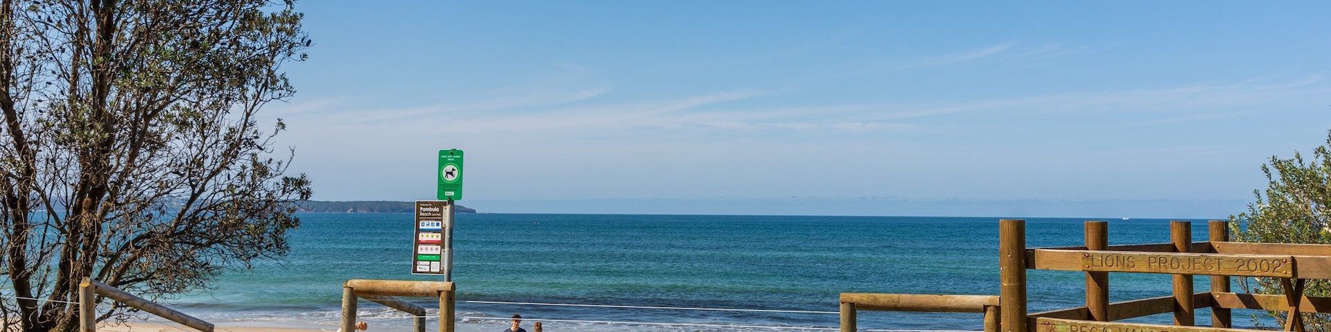 Uma praia com uma passarela de madeira, um poste de sinalização e vista clara do oceano.