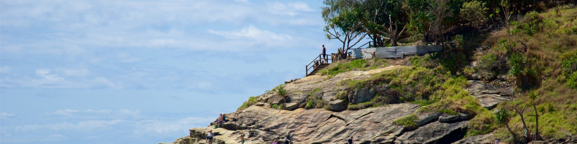 Uma praia rochosa com pessoas nadando e caminhando pela orla.
