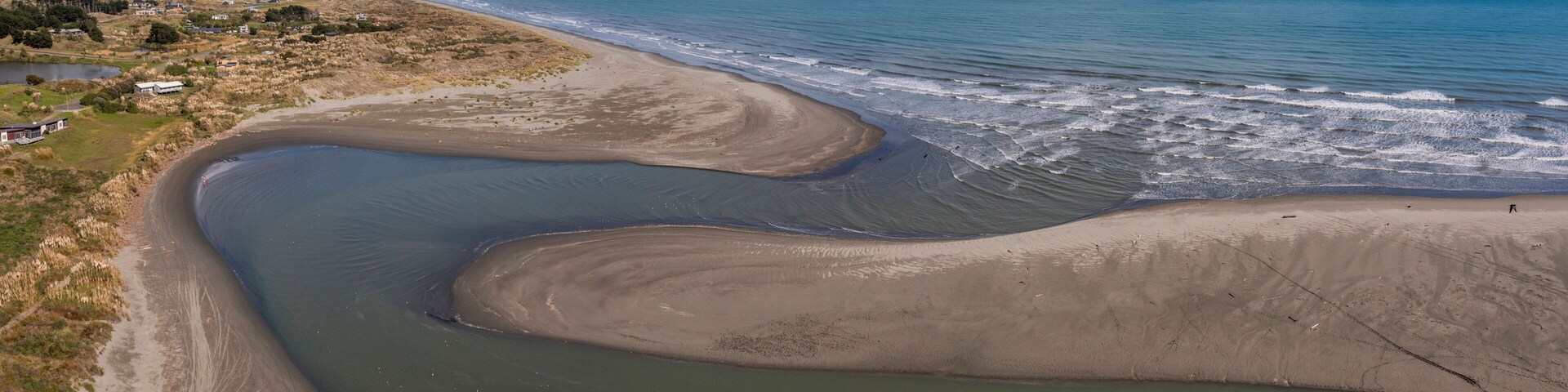Paisagem costeira com um rio sinuoso, praias arenosas e uma cordilheira ao longe.