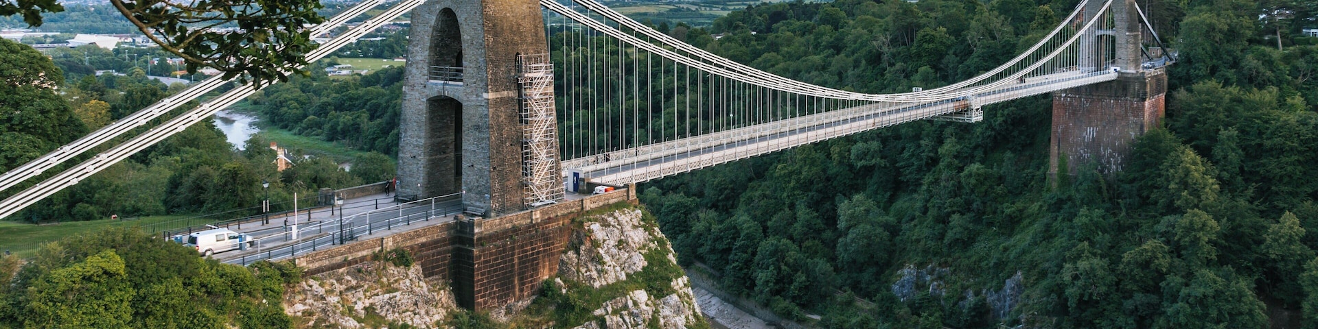 Uma ponte suspensa sobre um rio, cercada por vegetação exuberante e penhascos rochosos.