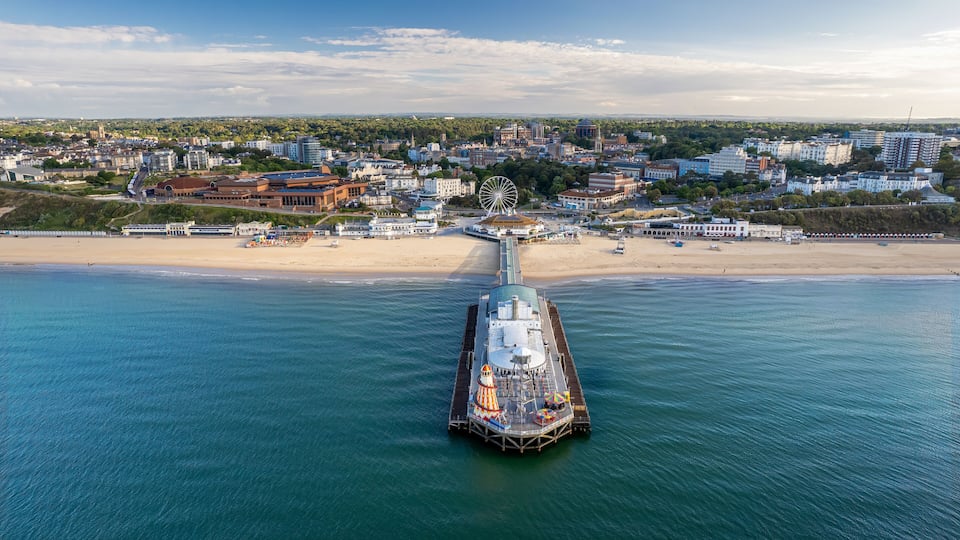 Um grande navio atracado em um cais, com uma praia e paisagem urbana ao fundo.
