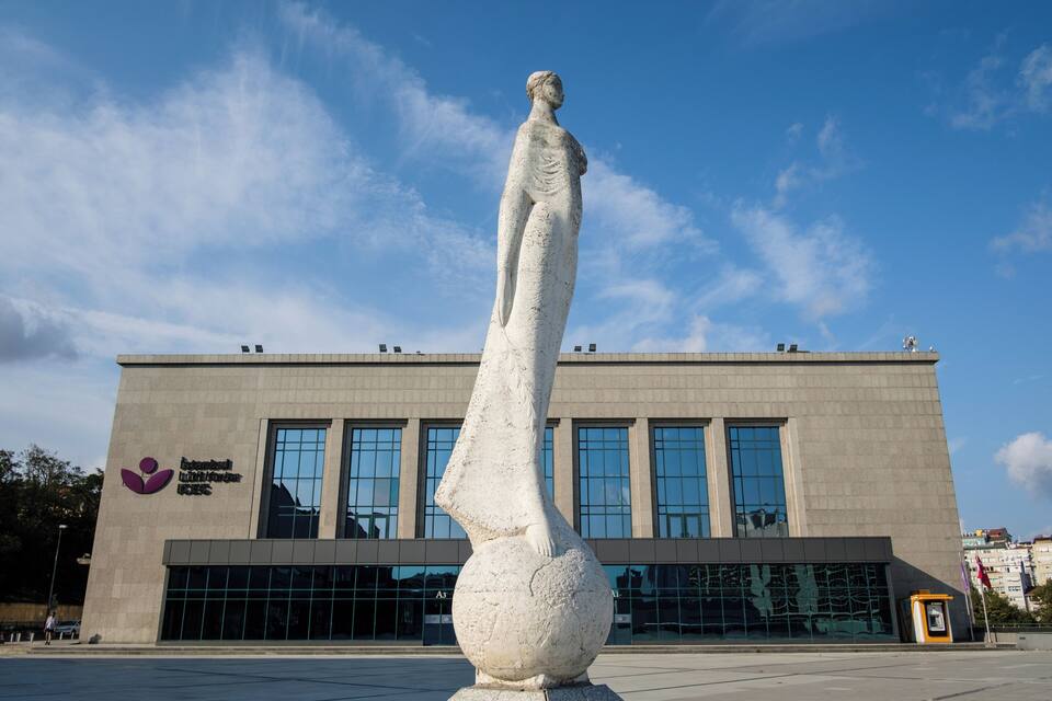 Uma estátua em frente a um edifício com grandes janelas e um logotipo à esquerda.