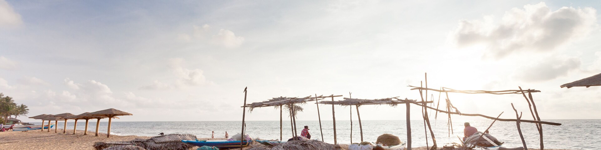 Uma praia com palafitas, barcos e mar calmo.