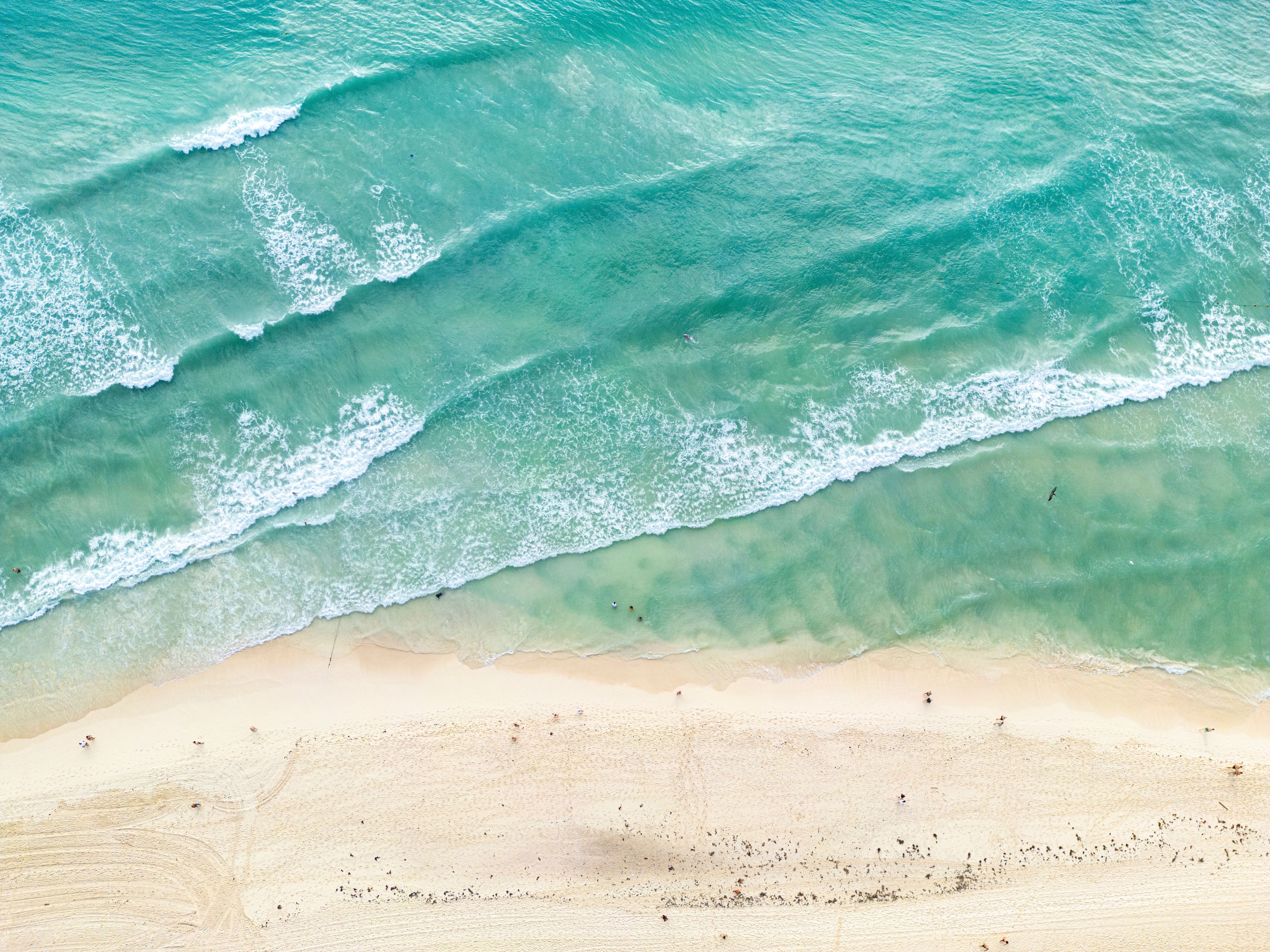 Oceano turquesa com ondas suaves e uma praia arenosa.