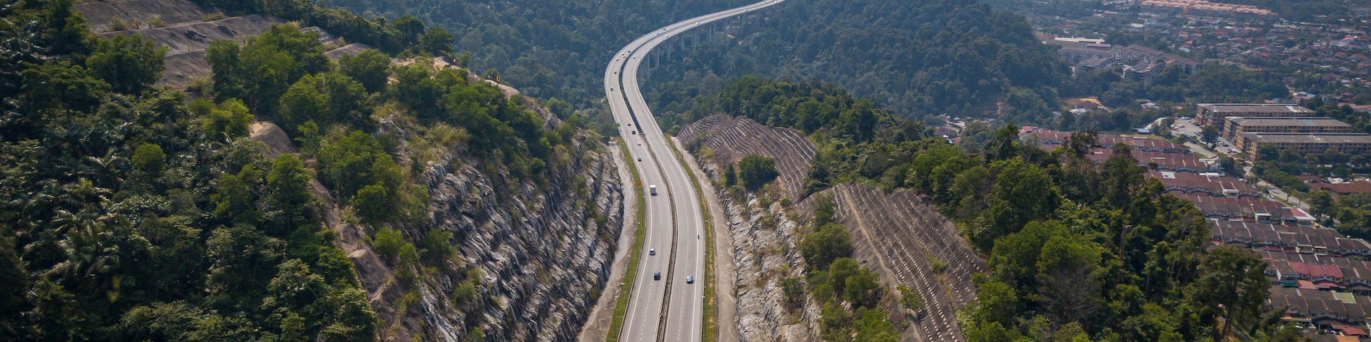 Uma estrada sinuosa serpenteando por uma região montanhosa, com florestas densas de ambos os lados.