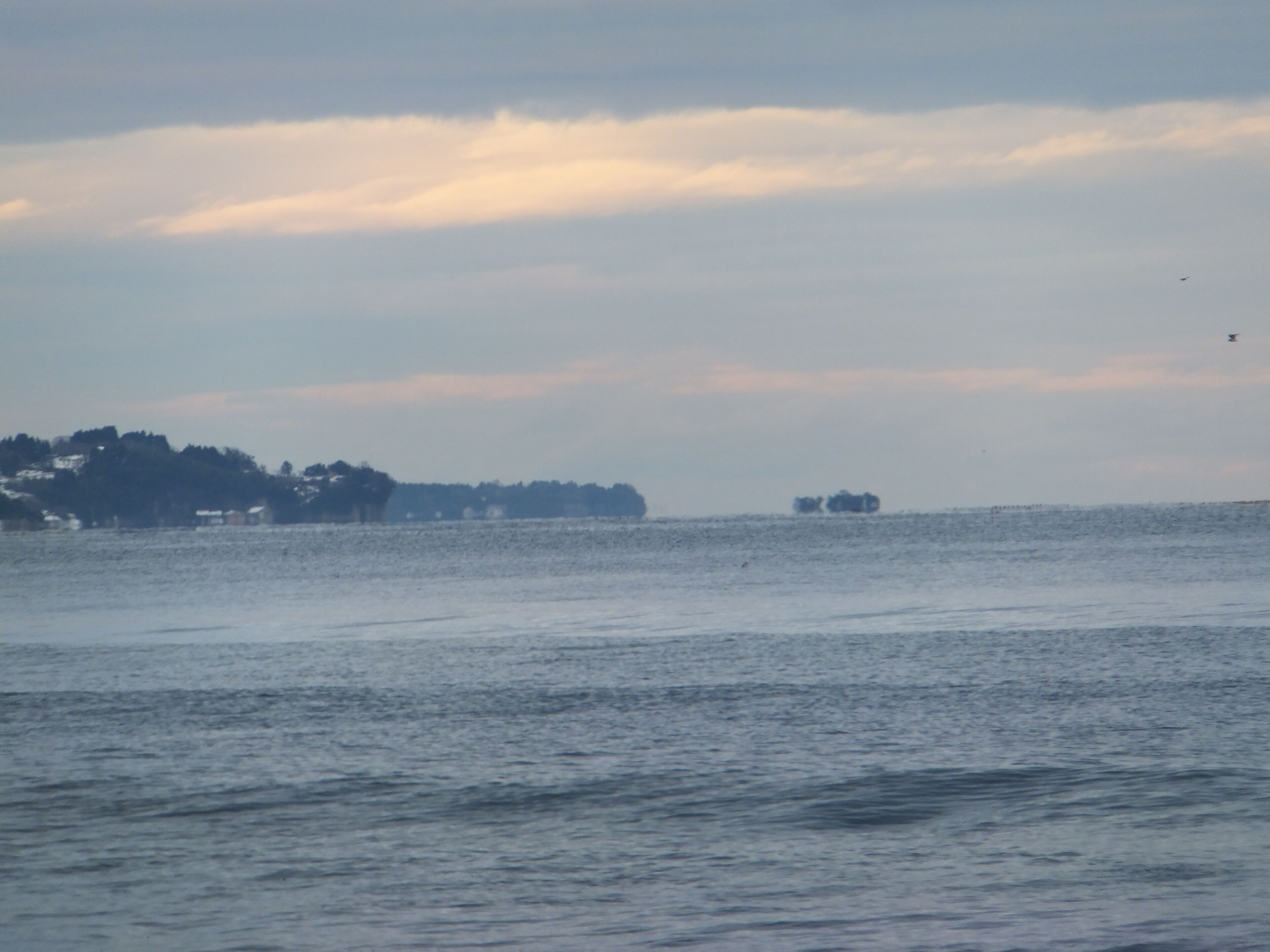 Mar calmo com uma linha de costa distante, um navio e um céu nublado.