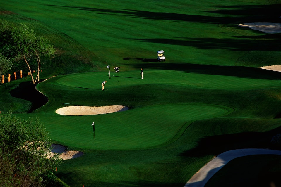 Campo de golfe com bunkers de areia, haste de sinalização e um carrinho de golfe branco.