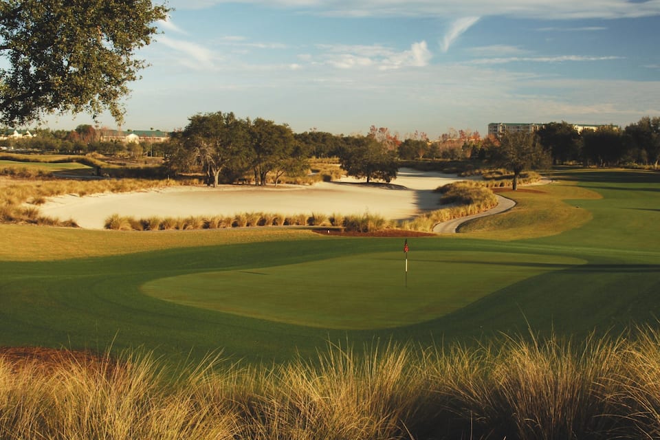Campo de golfe com bunkers de areia, árvores e mastro de sinalização.