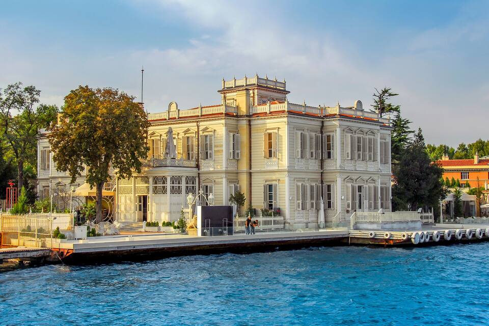 Um edifício histórico com fachada à beira-mar, grandes janelas e uma varanda com vista para a água.