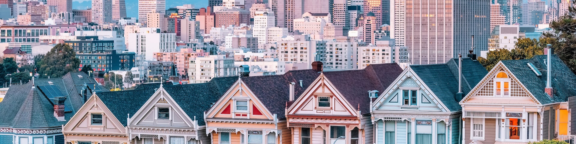Fileira de casas vitorianas em frente a um horizonte urbano com arranha-céus modernos.