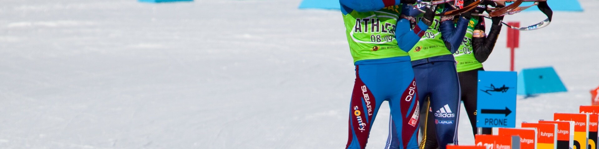 Esquiadores de fundo em movimento numa pista nevada com barreiras numeradas.