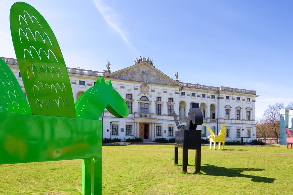 Uma grande escultura verde em frente a um edifício clássico com uma estátua no topo.