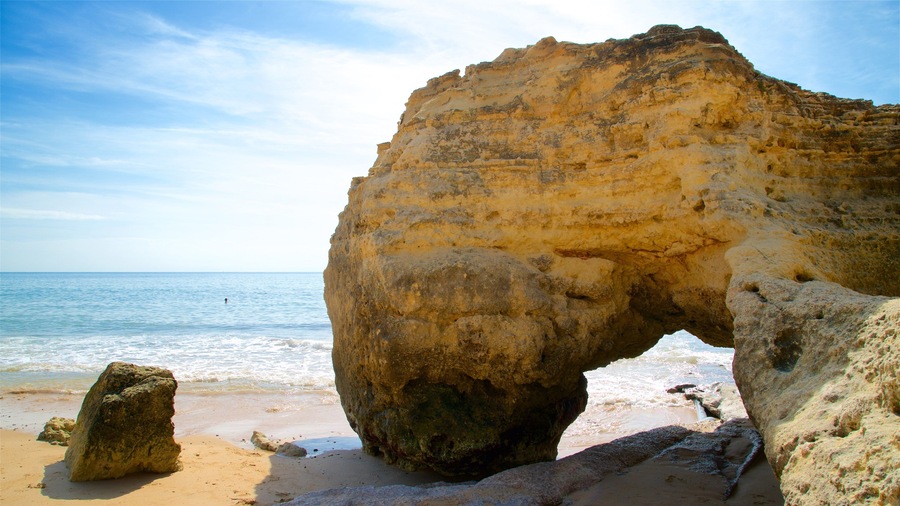 Uma grande formação rochosa numa praia, com o oceano ao fundo.