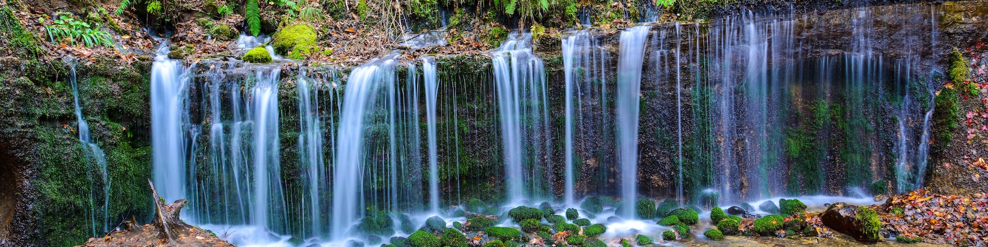 Uma cascata em vários níveis, com rochas cobertas de musgo e samambaias.