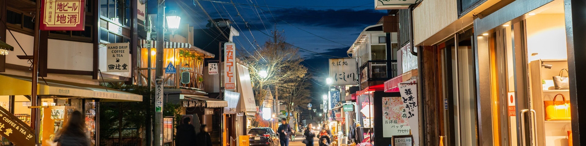 Uma rua à noite com letreiros iluminados, calçada de tijolos e pedestres.