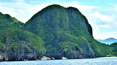 Paisagem costeira com uma colina verde destacada e um mar calmo.