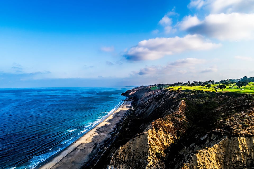 Paisagem costeira com praia, falésias e uma linha de costa distante.
