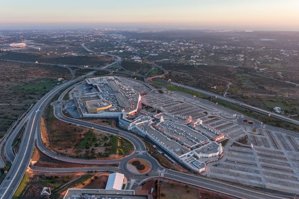 Vista aérea de um complexo entroncamento rodoviário com múltiplas rampas e viadutos, cercado por vegetação escassa e áreas urbanas ao longe.