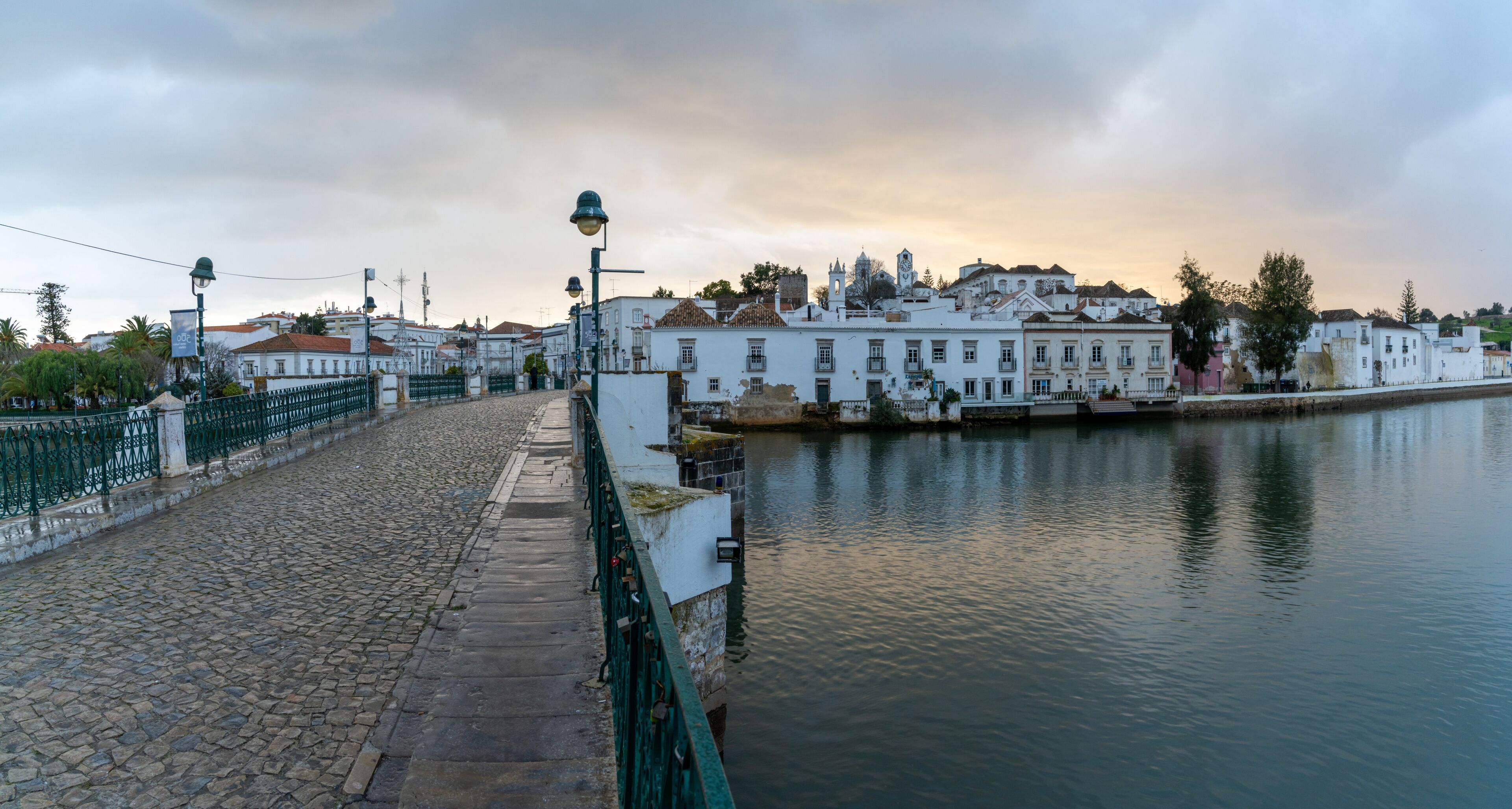 Um calçadão à beira-mar com edifícios históricos e uma grade de metal verde.