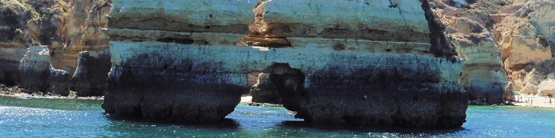 Formação rochosa costeira com um arco natural sobre águas azul-turquesa.