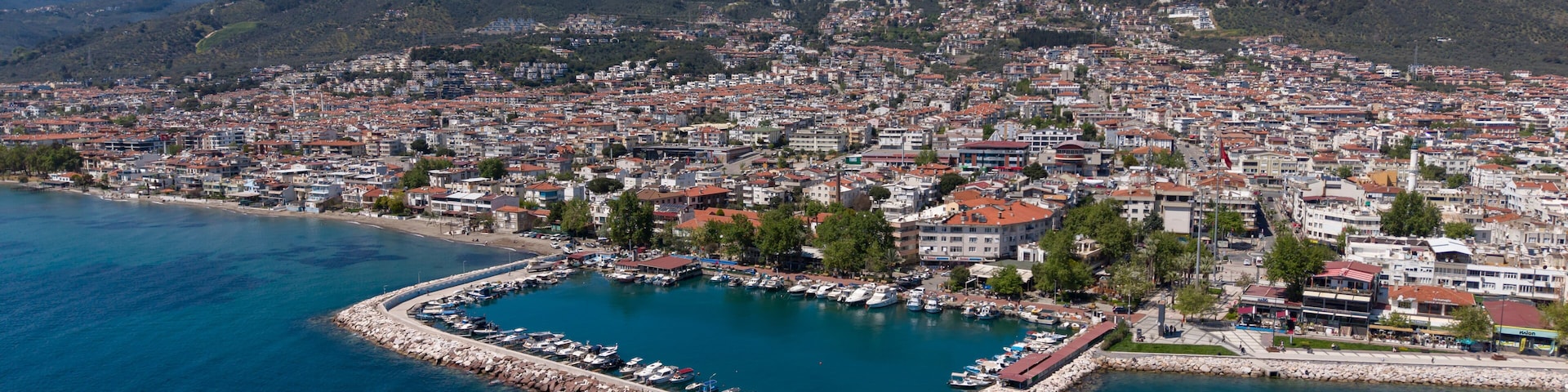Uma cidade costeira com um porto de recreio, área urbana densa e montanhas ao fundo.