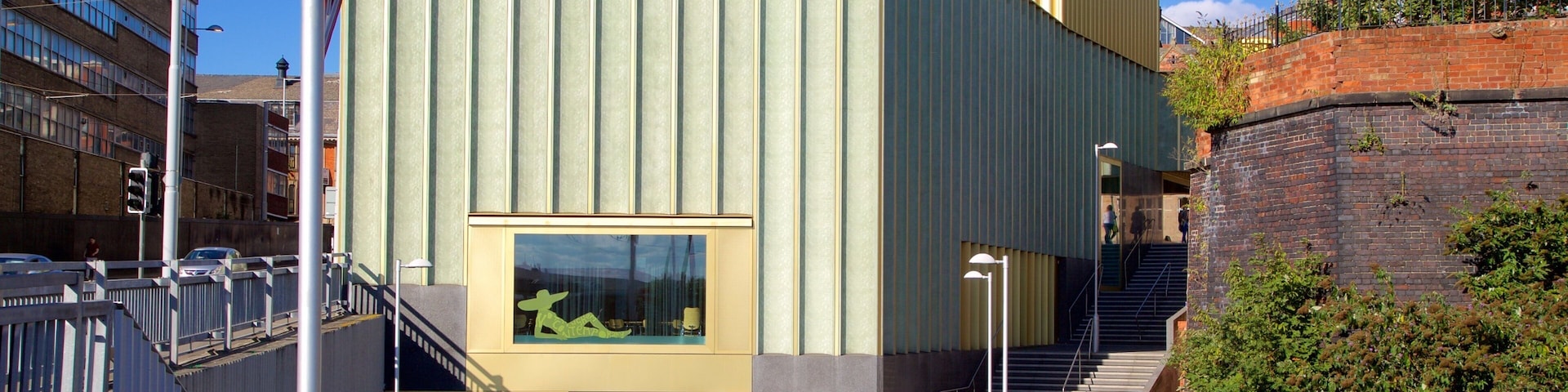 Um edifício moderno com fachada verde, um café chamado Cafe Bar e uma escadaria que leva a um nível superior.