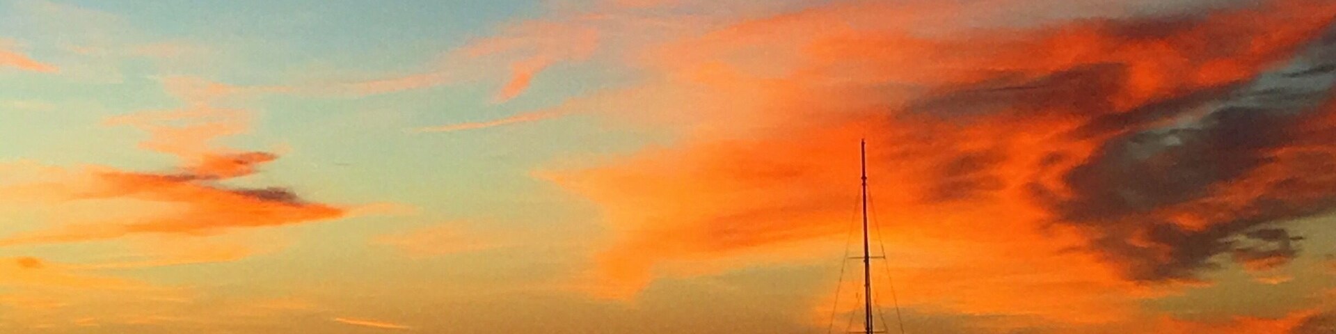 Um pôr do sol sobre um mar calmo, com um veleiro e um navio ao longe.