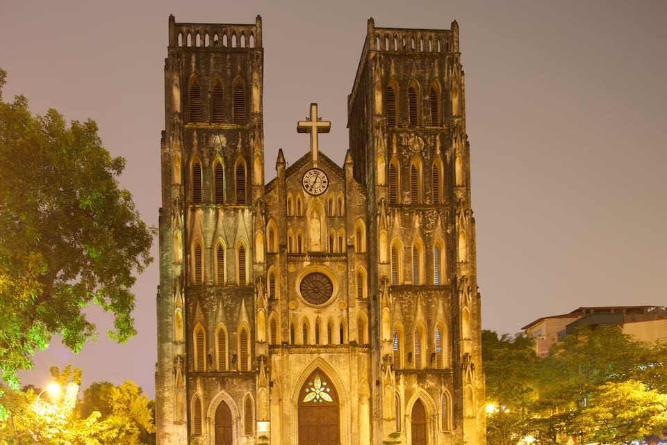 Uma catedral gótica com duas torres, uma rosácea e uma cruz no topo.