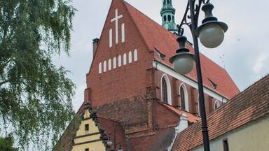 Uma igreja histórica com telhado vermelho e uma cruz na fachada, rua de paralelepípedos e um poste de luz.